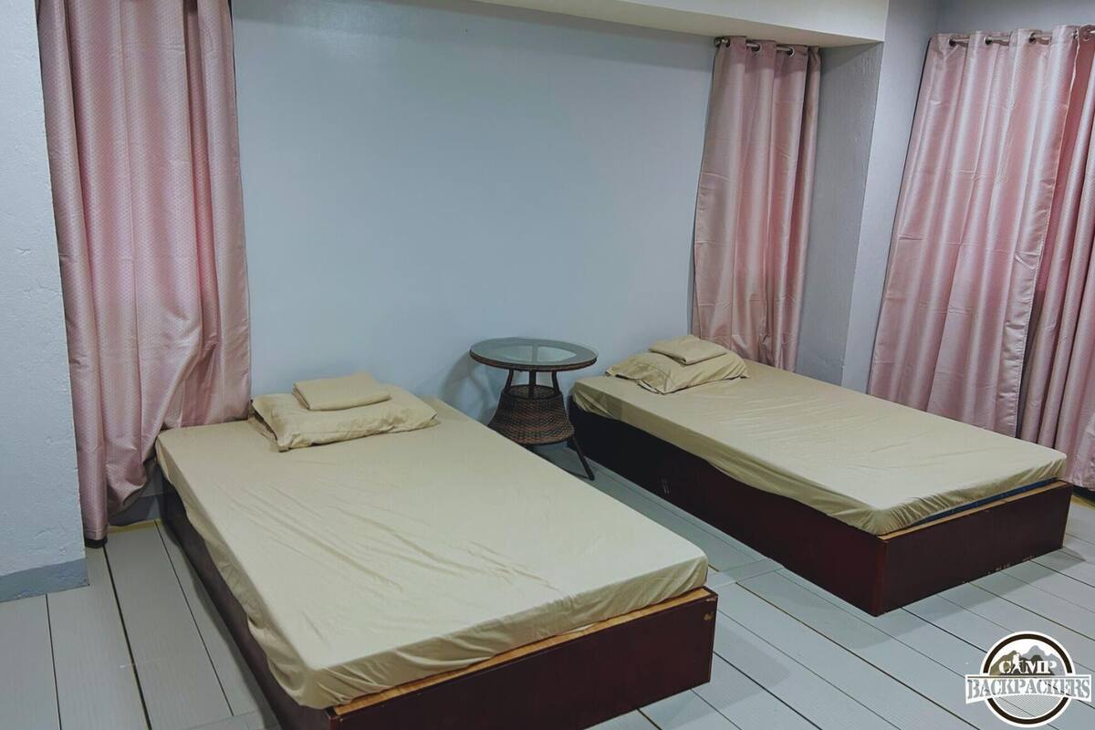 Quarto com duas camas, uma mesa redonda pequena e cortinas cor-de-rosa.