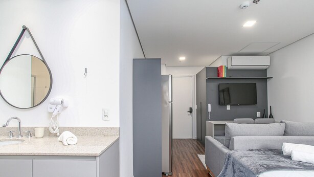 Quarto de hotel moderno com banheiro, cama, televisão e um pequeno espaço de estar.