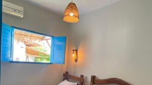 Quarto com duas camas, uma janela com persianas azuis, luminária pendente e aparelho de ar condicionado.