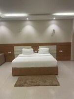 Quarto moderno com uma cama grande, cabeceira de madeira, tapete bege e iluminação embutida no teto.