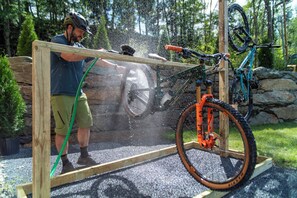 Uma pessoa limpando uma bicicleta em uma estrutura de madeira ao ar livre.