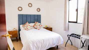 Um quarto com uma cama, mesa de cabeceira, janela com cortinas e uma cadeira.