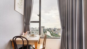 Uma sala de jantar com vista para a paisagem urbana através de uma grande janela, com uma mesa e cadeiras de madeira.
