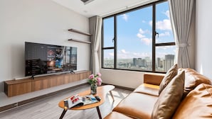 Uma sala de estar moderna com uma televisão grande, um sofá, uma mesa de centro com uma revista e um vaso de flores.