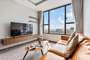 Uma sala de estar moderna com uma televisão grande, um sofá, uma mesa de centro com uma revista e um vaso de flores.