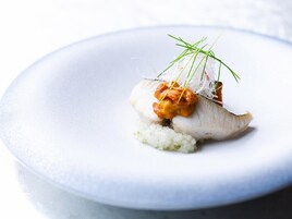 Prato branco com um pedaço de peixe branco coberto com molho laranja e adornado com ervas verdes.