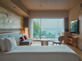 Quarto de hotel com uma cama grande, sofá, escrivaninha, televisão e varanda com vista.