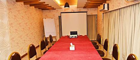 Uma sala de conferências com uma mesa comprida, cadeiras, tela de projetor e aparelho de ar condicionado.