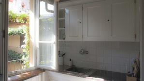 Uma cozinha com armários brancos, bancada de granito, pia de aço inoxidável e janela com vista para um jardim.