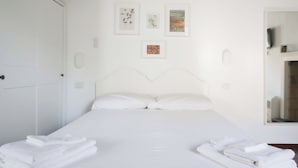 Um quarto branco com uma cama, uma porta e três quadros na parede.