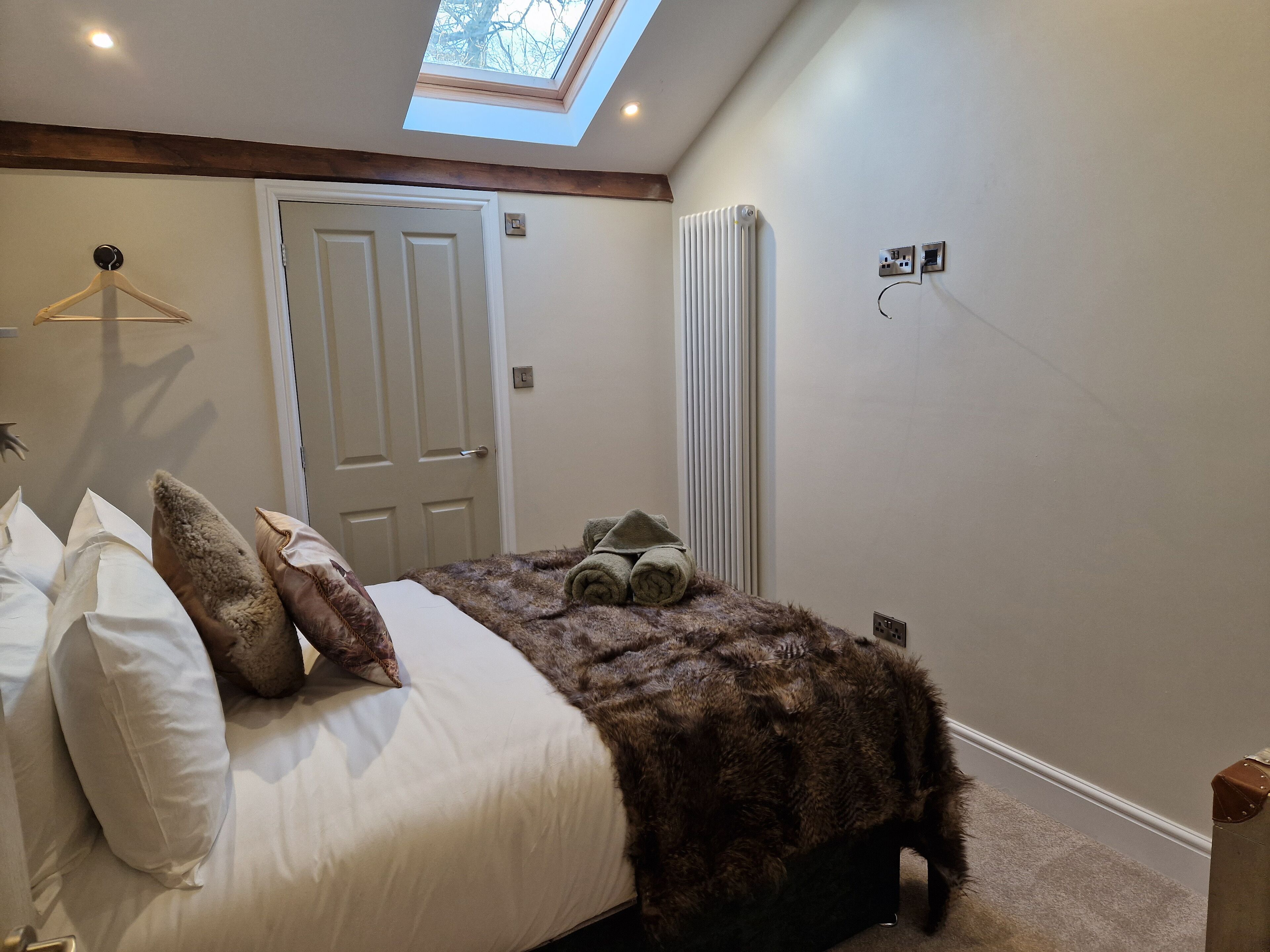 Um quarto com cama, claraboia, radiador e porta.