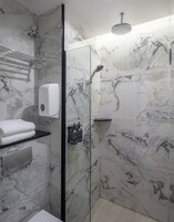 Um banheiro moderno com chuveiro em gabinete de vidro, paredes de mármore, porta-toalhas e dosador de sabonete.