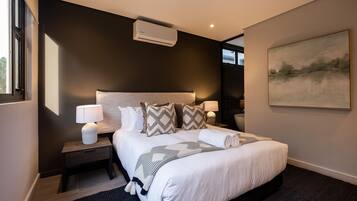Quarto de hotel moderno com uma cama grande, uma mesa de cabeceira com luminária, ar condicionado fixado na parede e um quadro na parede.