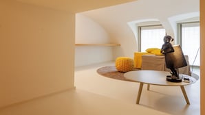 Quarto moderno e bem iluminado, com uma mesa redonda, uma luminária e um sofá com almofadas.