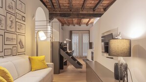 Uma sala de estar moderna com uma escada que leva a uma cozinha, obras de arte nas paredes e uma luminária em uma mesa lateral.