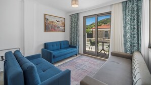Uma sala de estar moderna com um sofá azul, um sofá cinza e uma grande janela com vista para um edifício e colinas.