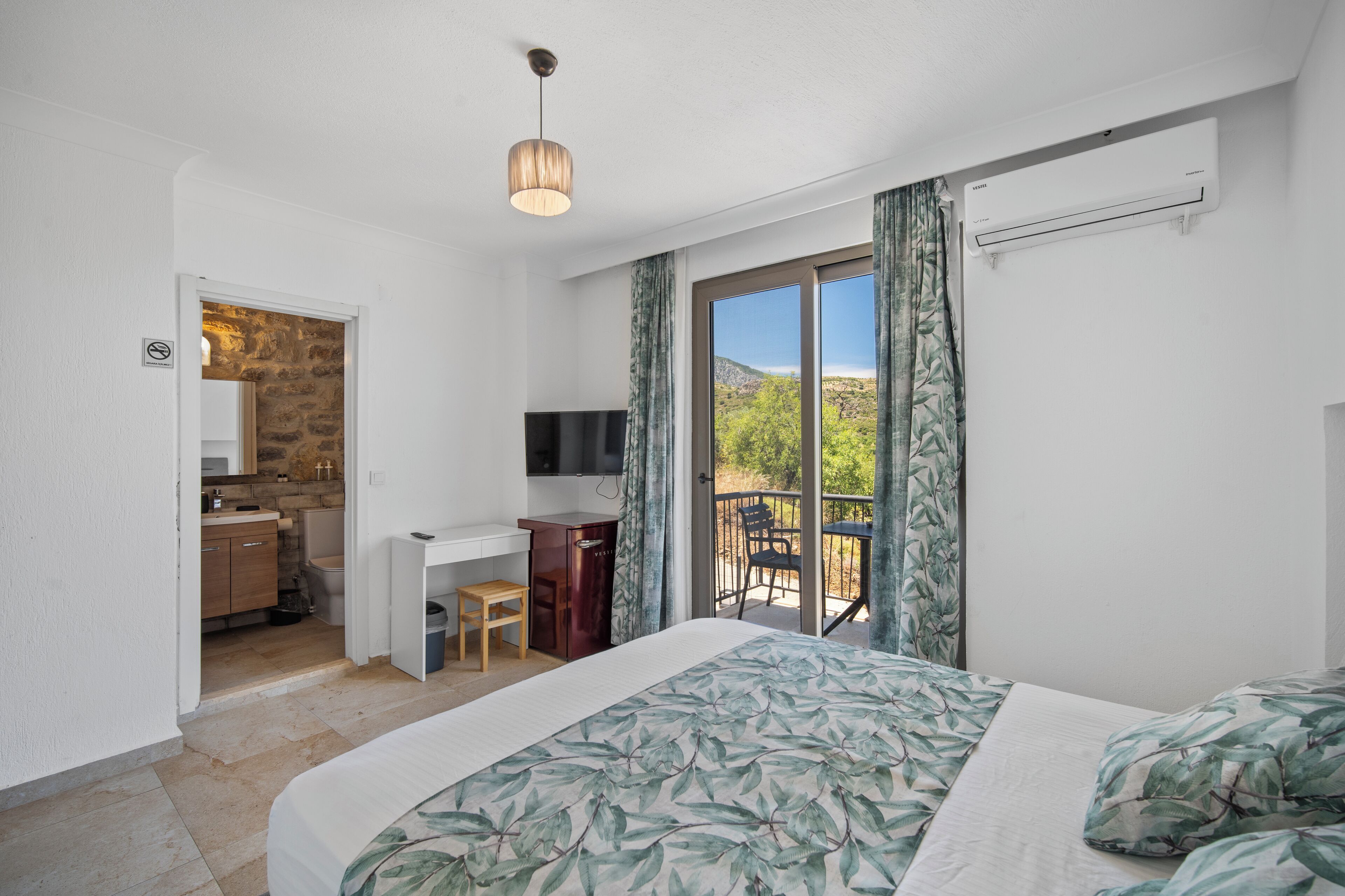 Quarto com cama, escrivaninha, televisão e varanda com vista para o exterior.