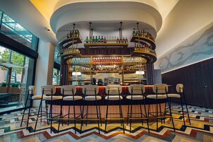 Uma área de bar com várias prateleiras de garrafas, banquetas e um chão estampado.