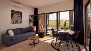 Sala moderna com sofá, mesa de centro e área de jantar com cadeiras. Há uma janela grande com vista para o exterior.