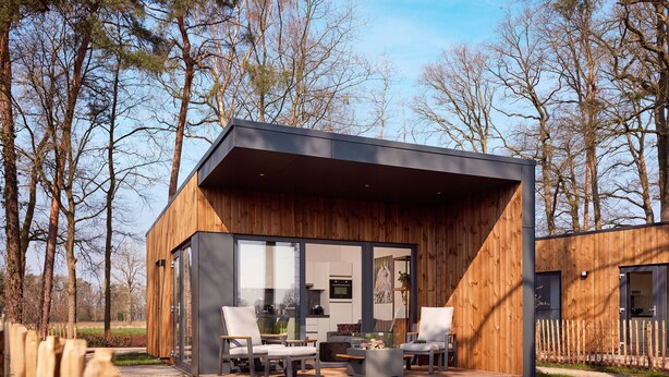 Uma cabana moderna de madeira com um alpendre envidraçado, mobiliada com cadeiras e uma mesa.