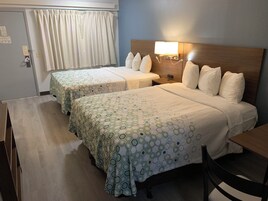Quarto de hotel com duas camas, uma escrivaninha, uma cadeira e uma mesa de cabeceira.