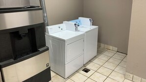Uma área de lavanderia com máquina de lavar e secadora, aquecedor de água e piso revestido de azulejos.