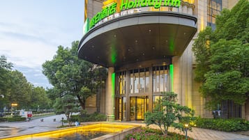 Entrada de hotel com fachada curva, colunas imponentes e boa iluminação.