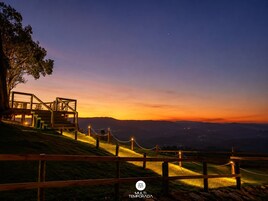 Um deque de madeira com cerca de arame, com vista para uma paisagem montanhosa ao crepúsculo.