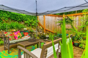 Uma área de varanda coberta com um banco de madeira, uma mesa e diversos vasos de plantas.