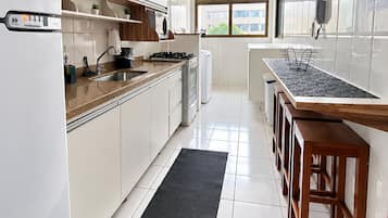 Cozinha moderna com armários brancos, tapete preto e um banco de madeira.