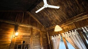 Interior de madeira com ventilador de teto, luminária pendente e vista pela janela com cortinas.