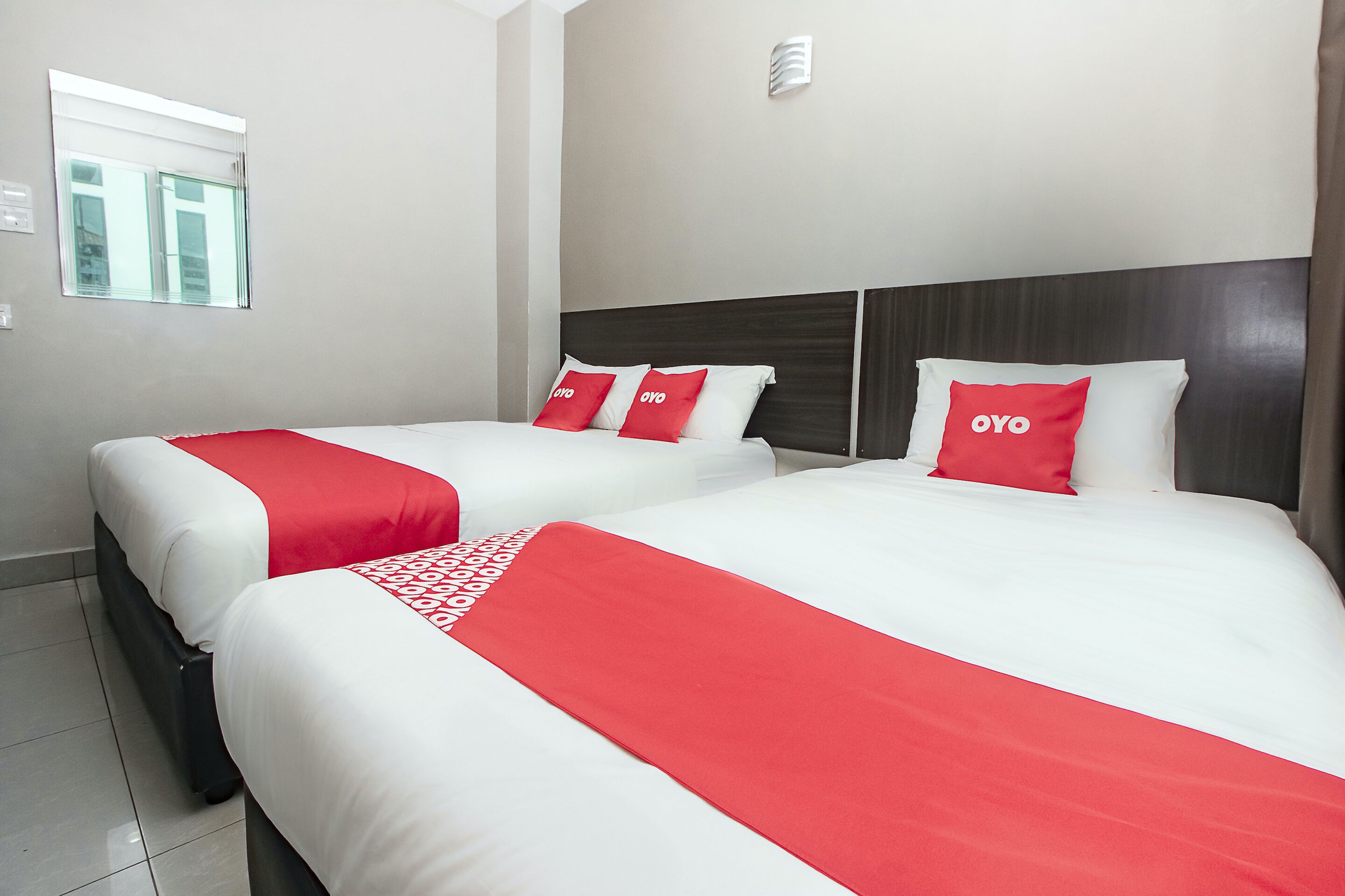 Quarto de hotel com duas camas, cada uma com roupa de cama branca e vermelha, e uma janela com persianas.