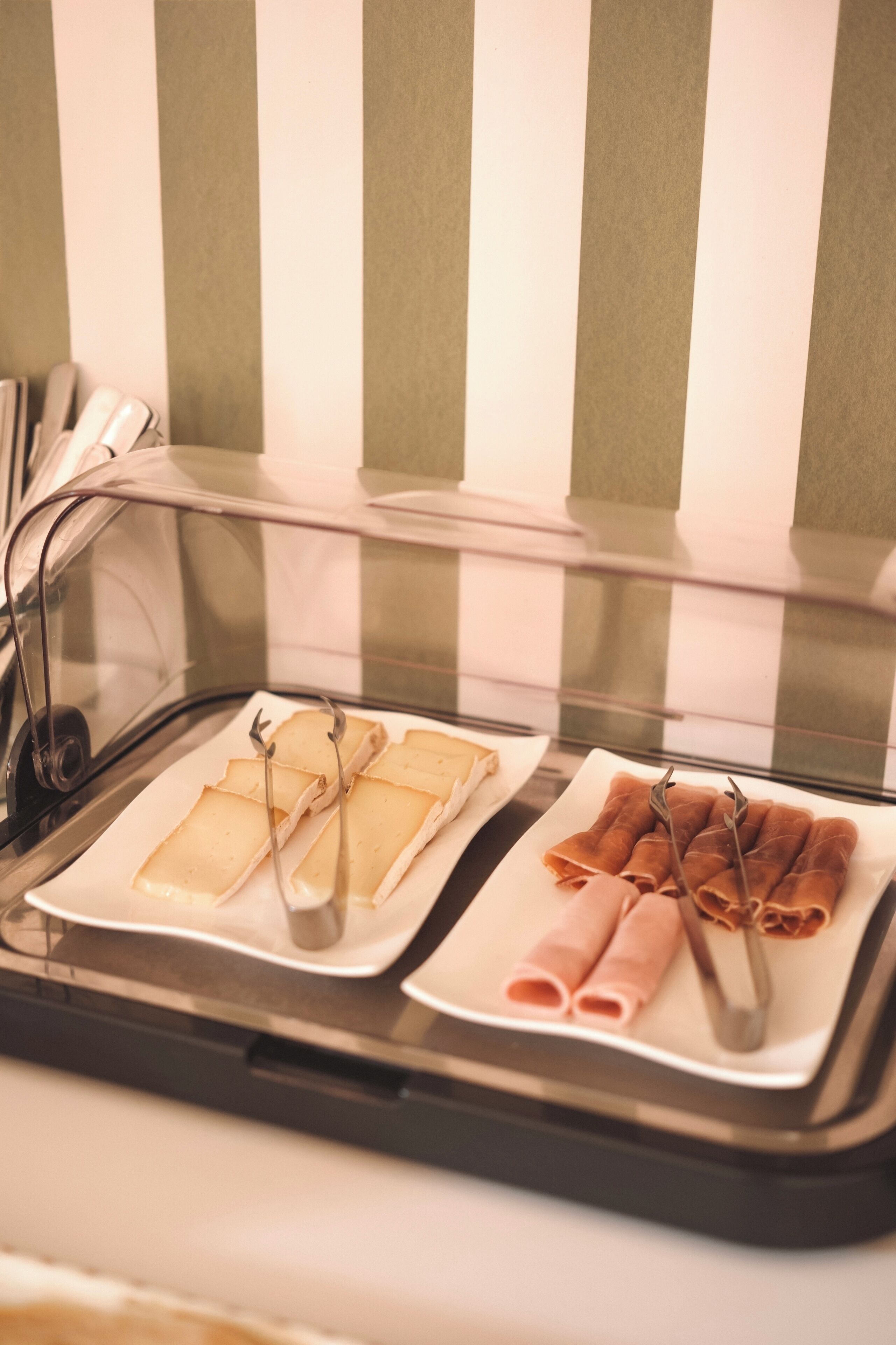 Buffet com diversos alimentos, incluindo panquecas e carnes enroladas, expostos em uma área de serviço coberta por vidro.