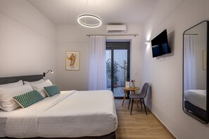 Quarto de hotel com cama, escrivaninha, cadeira, televisão e um espelho grande.