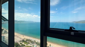 Vista de uma área costeira com uma praia, céu claro e uma cordilheira distante.