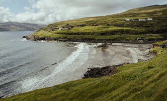 Paisagem costeira com colinas gramadas, uma praia e casas.