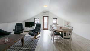 Um apartamento loft moderno com pé-direito alto, área de jantar com cadeiras de madeira, TV e uma janela grande.