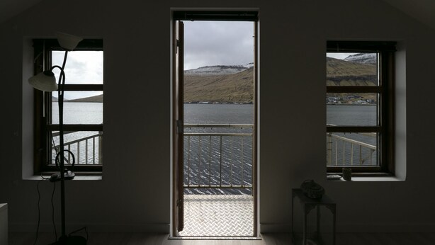 Quarto com vista para um lago e montanhas, porta que dá para o exterior e uma luminária de chão.
