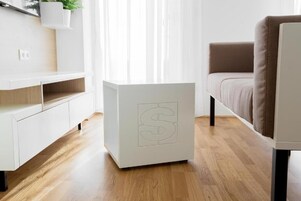 Uma sala de estar moderna com um armário branco, uma mesinha lateral com um logotipo, um sofá marrom e piso de madeira.