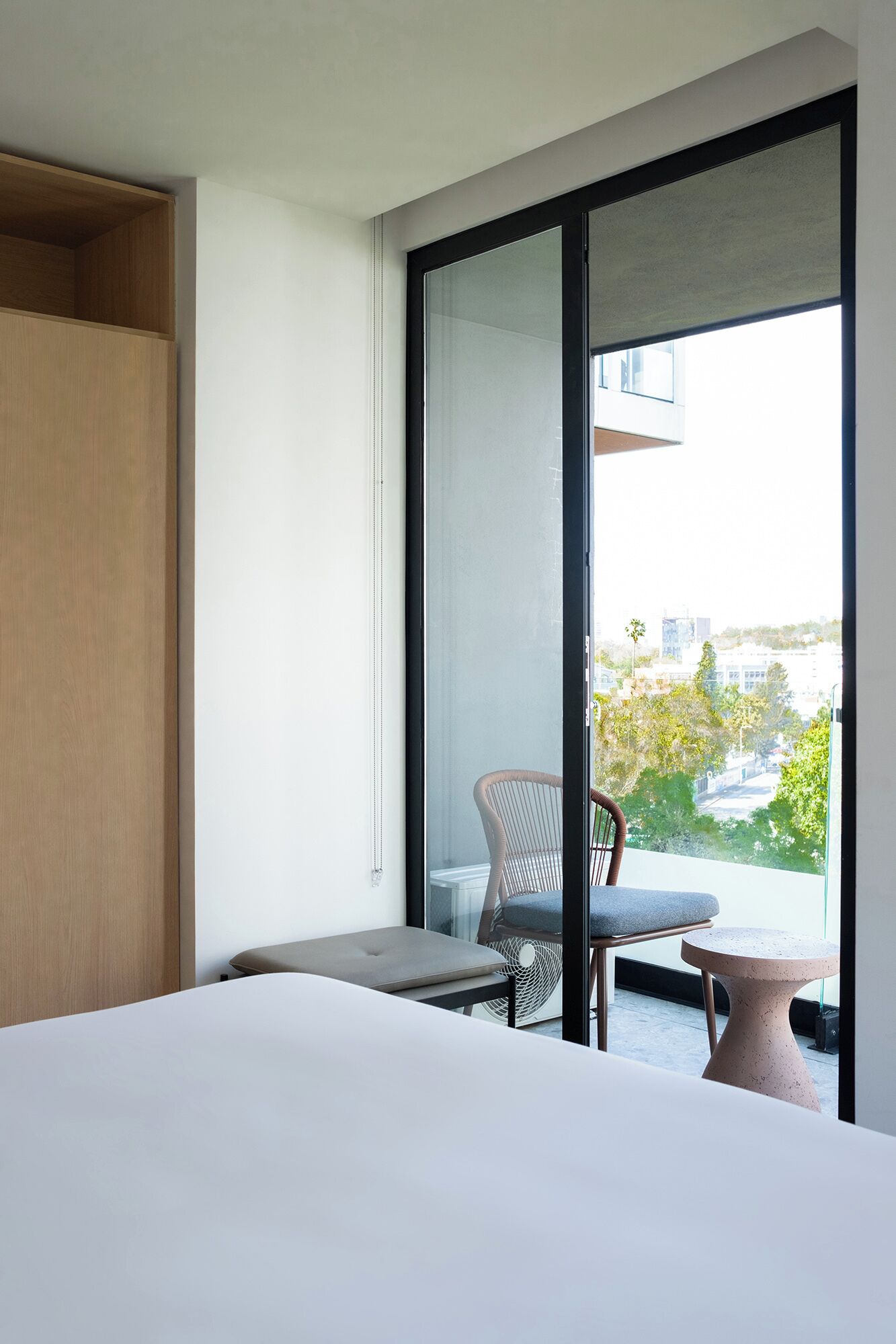 Quarto de hotel com cama, cadeira, mesa pequena e varanda com vista para a cidade.