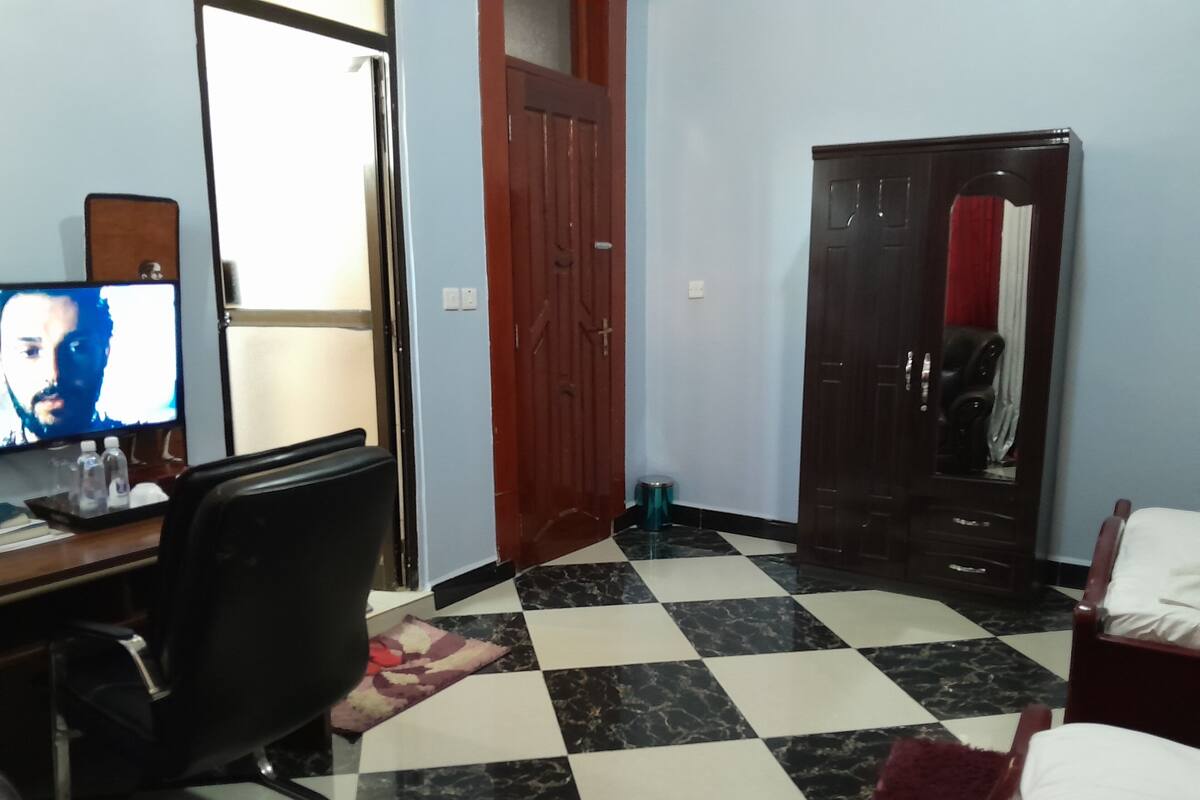 Quarto com piso xadrez, escrivaninha com computador, cadeira, armário e cama.