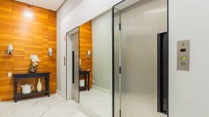 Um elevador moderno com tela digital, painel de controle e espelho na parede.