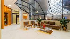 Um interior moderno com teto de vidro, um sofá, cadeiras, uma mesa de centro e plantas em vasos.