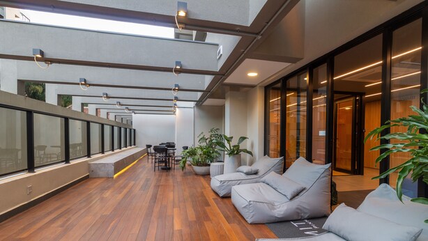 Um espaço interior moderno com piso de madeira, área de estar com almofadas e plantas em vasos.