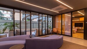 Uma sala de estar moderna com um sofá roxo curvo, uma mesinha redonda e um painel de vidro com vista para o exterior.