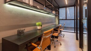 Uma sala de conferências com uma mesa comprida, cadeiras, uma planta em vaso e livros nas estantes.