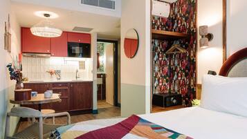 Quarto de hotel com uma cama, uma escrivaninha com cadeira, uma cozinha compacta e um banheiro.
