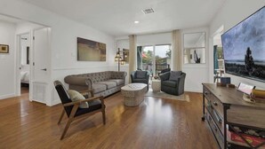Uma sala de estar espaçosa com um sofá grande, duas poltronas, uma mesa de centro e uma televisão de tela plana.