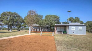 Uma área cercada com um caminho de terra, um pequeno edifício com garagem e árvores ao fundo.