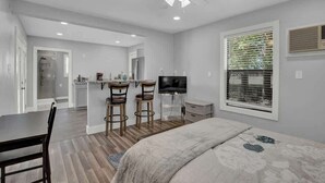 Um quarto com cama, escrivaninha, televisão e janela com persianas.